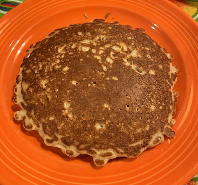 Golden-brown perfection on an orange plate—this pancake has achieved what many politicians can't: being both substantial and light simultaneously.