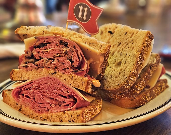 The pastrami sandwich stands tall like a meaty skyscraper between rye bread foundations. That little flag isn't decoration – it's claiming territory in your heart.