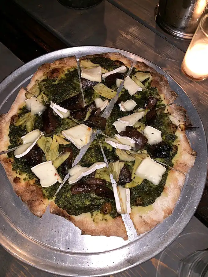 This isn't just pizza—it's a garden party on a crust, where pesto plays host and artichokes mingle with perfectly melted cheese.
