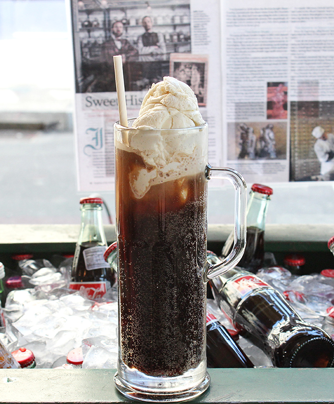 The root beer float: where carbonation meets creaminess in a tall glass tango. Those vintage bottles in the background aren't just decoration—they're co-conspirators.
