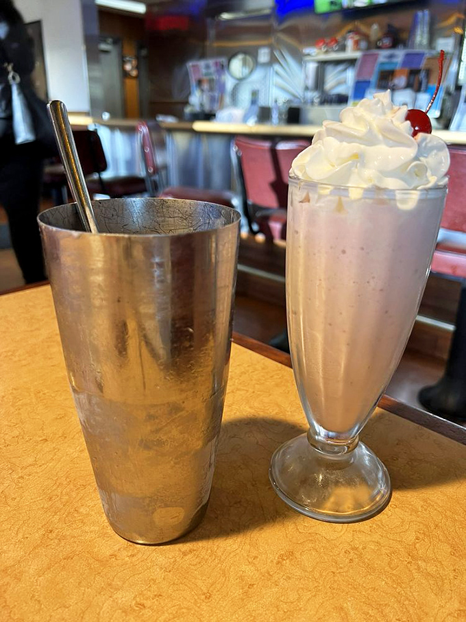 The classic diner milkshake arrives with its metal sidekick—whipped cream piled high, cherry on top, and enough thickness to challenge your straw's resolve.