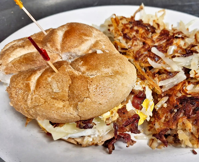 Breakfast architecture at its finest—a perfectly constructed sandwich with crispy bacon and melty cheese, alongside hash browns that mean business.