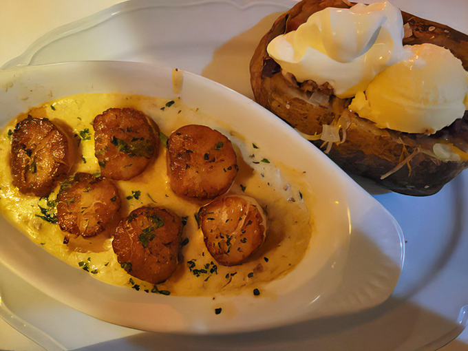These golden-seared scallops swimming in butter sauce aren't just seafood—they're little ocean medallions of happiness served alongside a potato that's dressed better than most people.