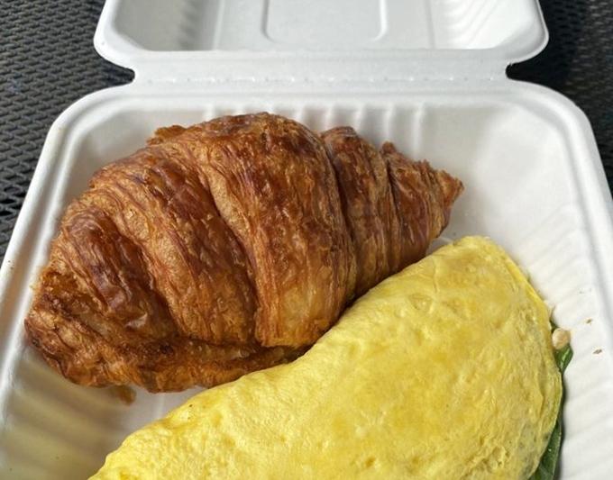 The humble croissant, achieving its highest purpose alongside a perfectly executed omelet. Butter-crafted poetry on a takeout container.