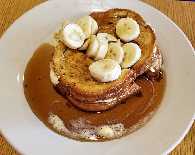 French toast that's achieved celebrity status, crowned with fresh banana slices and swimming in maple syrup. This isn't breakfast—it's dessert with permission.