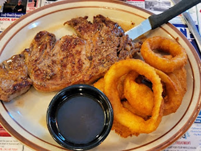 This isn't just a steak—it's a commitment. Golden onion rings and a side of dipping sauce complete this plate of pure satisfaction.