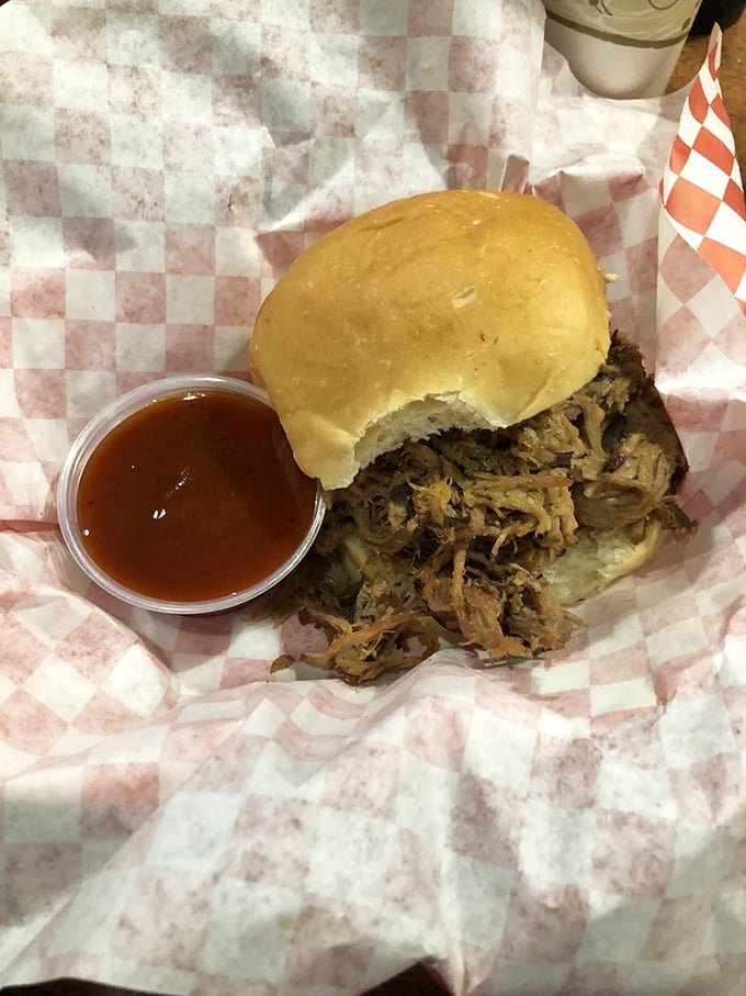 A pulled pork sandwich so tender it practically surrenders to gravity. That sauce cup isn't optional—it's your ticket to flavor paradise.