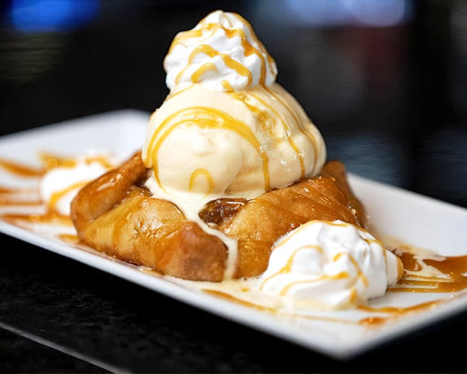 Dessert architecture at its finest—vanilla ice cream crowning golden-fried apple tarts, all drizzled with caramel that cascades down like sweet, edible lava.