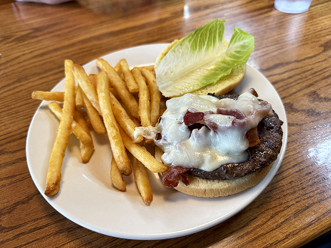 This isn't just a burger—it's architecture. Melted cheese cascades over bacon and beef like a dairy waterfall, with golden fries standing at attention nearby.