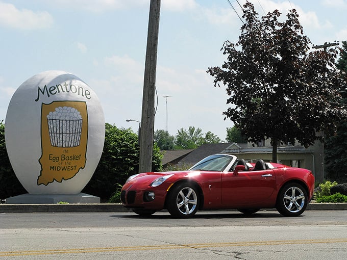 The sleek sports car provides perfect scale comparison to Mentone's oversized egg – speed meets whimsy at this Indiana intersection.