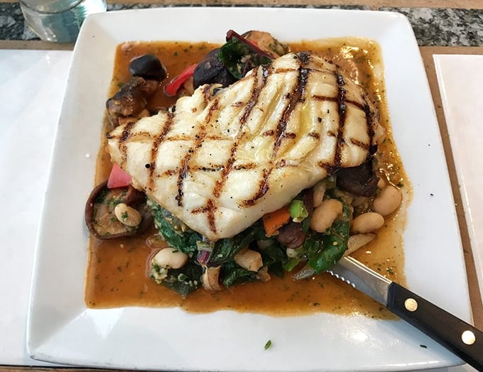 Perfectly grilled black cod rests atop a vibrant medley of vegetables. The crosshatch grill marks aren't just for show—they're flavor's signature.