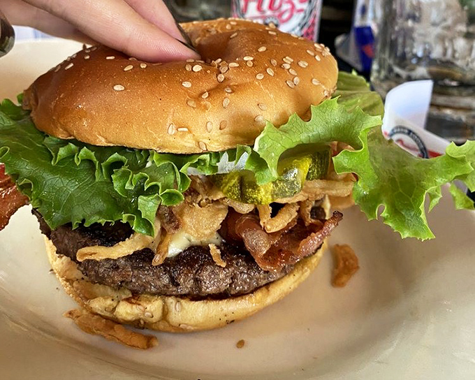 A burger that demands a jaw unhinging like a python—stacked with crispy onions, bacon, and fresh lettuce on a perfectly toasted sesame bun.