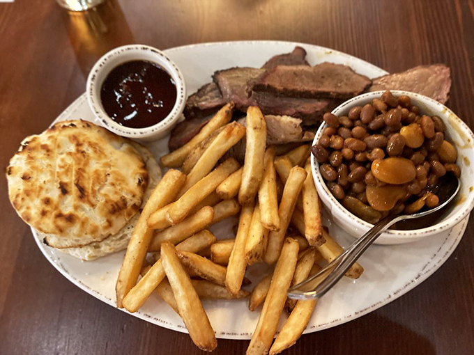 The holy trinity of BBQ sides—golden fries, savory beans, and a buttery biscuit—flanking slices of brisket with that telltale pink smoke ring of perfection.