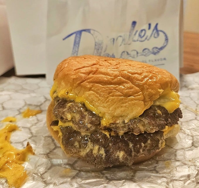 Behold the double cheeseburger in its natural habitat. Two beef patties melting into American cheese on a potato bun – comfort food that speaks a universal language.