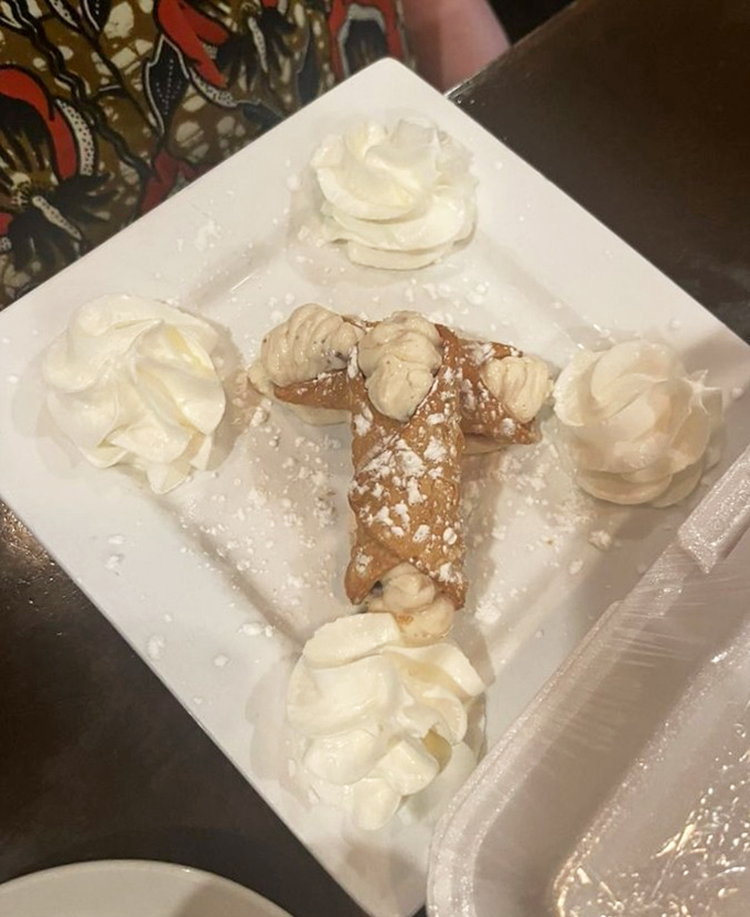 This cannoli isn't just dessert, it's edible architecture – a crisp shell fortress protecting the sweetened ricotta treasure within, surrounded by whipped cream sentinels.