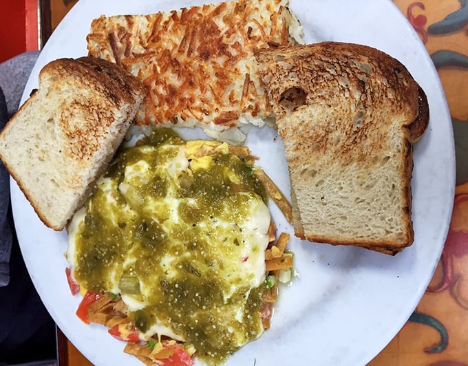 Green salsa cascades over eggs nestled among fresh vegetables—a California twist on breakfast that makes ordinary toast blush with inadequacy.