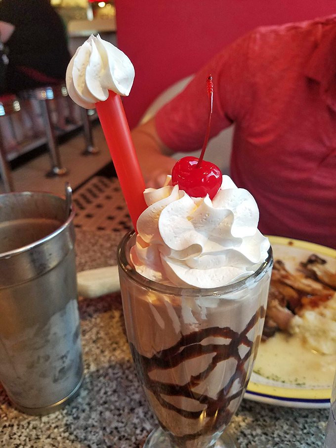 The chocolate malt arrives with whipped cream mountains and that signature metal mixing cup on the side – because one glass of heaven is never enough.