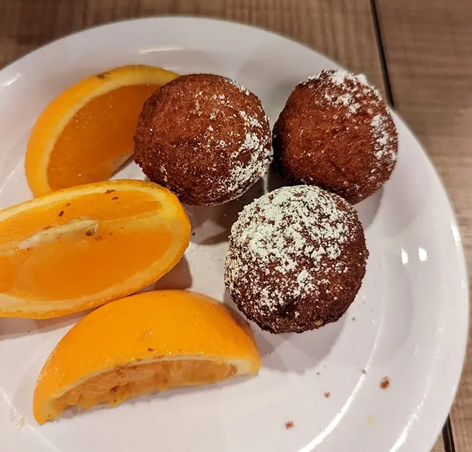 These donut holes aren't just treats—they're edible welcome mats, dusted with powdered sugar and served with orange slices for that vitamin C alibi.
