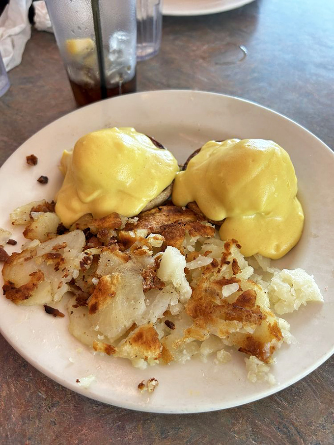 Eggs Benedict done right—golden hollandaise cascading over perfectly poached eggs. The crispy home fries are playing no supporting role here.