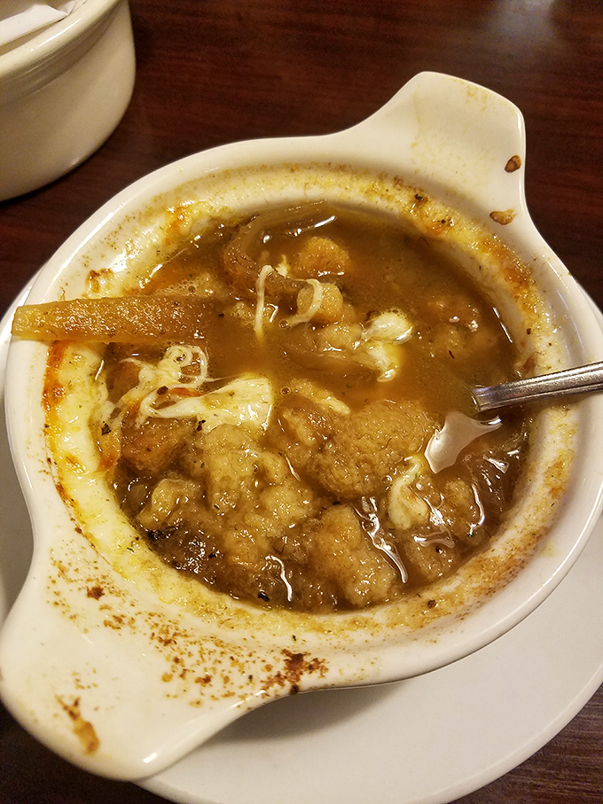 The legendary French onion soup—where caramelized onions swim in rich broth beneath a canopy of melted cheese that stretches with each spoonful like nature intended.