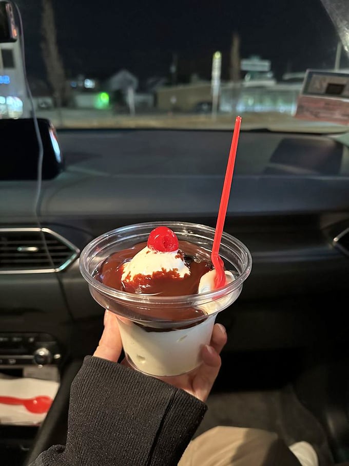 Hot fudge cascading over vanilla custard like chocolate lava, topped with that signature maraschino cherry. Car dashboard dining at its finest.