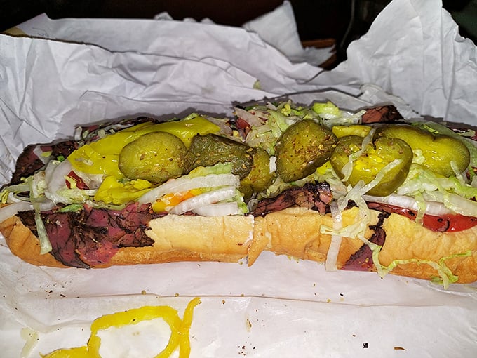 This sandwich isn't just wearing a pickle hat—it's sporting the entire produce department. The mustard drip tells you it's going to require napkins. Many napkins.