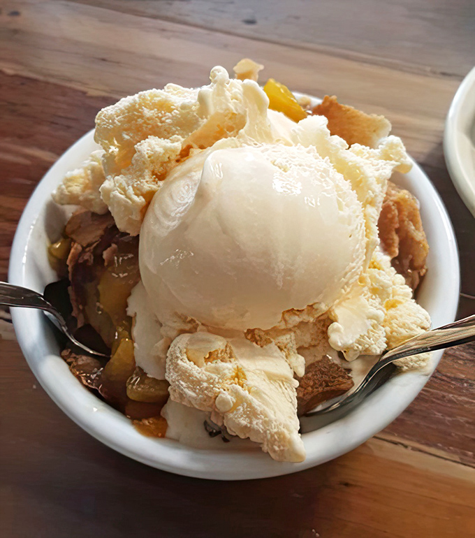 Ice cream melting into warm peach cobbler creates that perfect hot-cold romance – like summer and fall decided to have a delicious little affair on your plate.