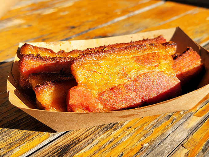 The pork belly glistens in the sunlight like edible stained glass—crispy, caramelized edges giving way to succulent meat that melts faster than your willpower.