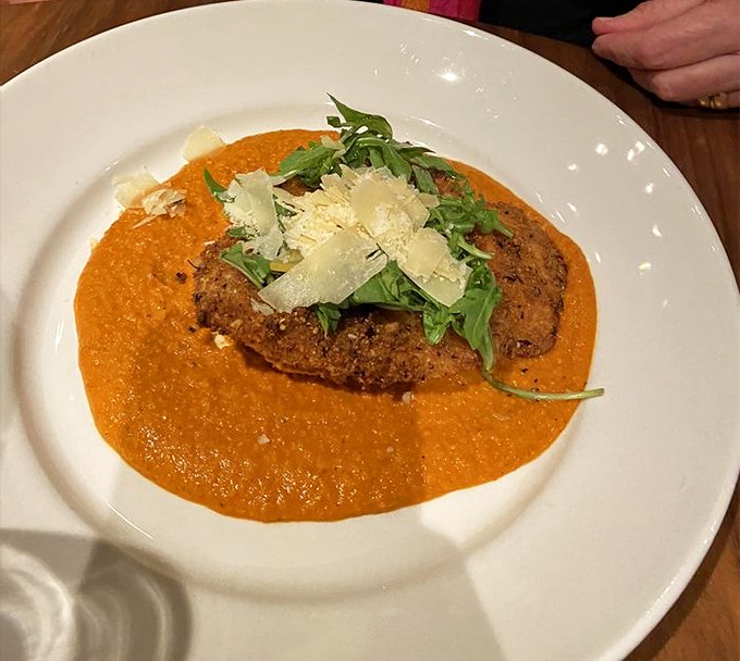 The Tavern Chicken basks in a vibrant orange Romesco sauce, topped with fresh arugula and Parmesan—comfort food dressed for a night out.