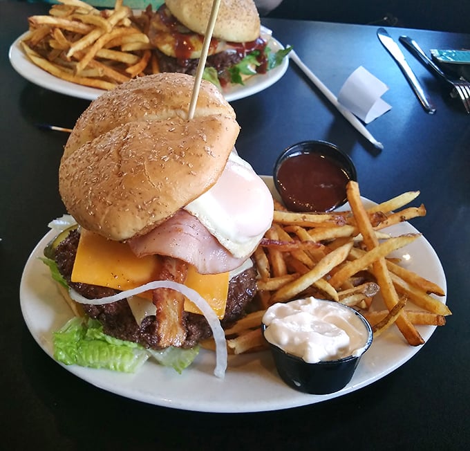 Behold the burger in its natural habitat—accompanied by golden fries and house-made dipping sauces. The toothpick isn't decoration; it's structural engineering for this towering masterpiece.