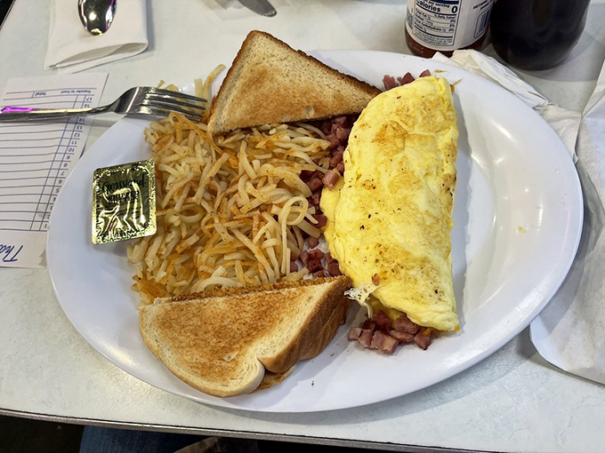 The Western omelet—a golden envelope of eggs stuffed with ham and perfectly melted cheese—flanked by crispy hash browns and toast soldiers ready for action.