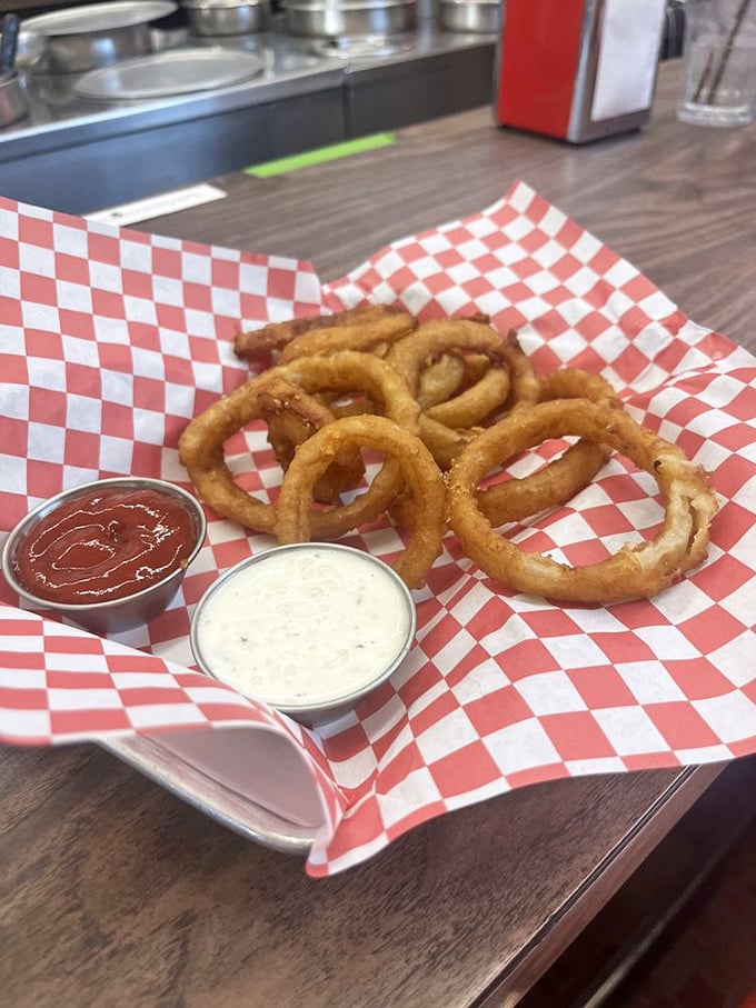 Golden onion rings that crackle with each bite, served with dipping sauces in red checkered baskets—diner perfection that needs no filter.