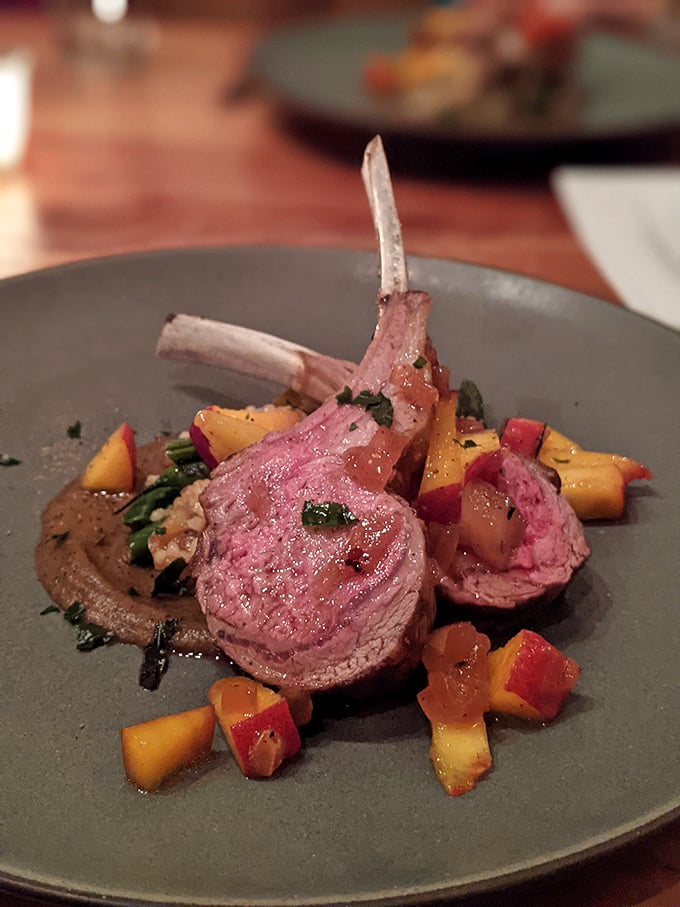 Lamb chops presented like the crown jewels they are. Pink, perfect, and positioned atop seasonal vegetables that aren't just garnish—they're part of the story.
