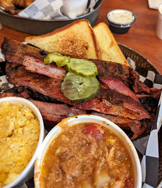 Ribs displaying that perfect "kiss of smoke" complexion, with sides standing by for moral support. That pickle isn't decoration—it's a palate-cleansing necessity.