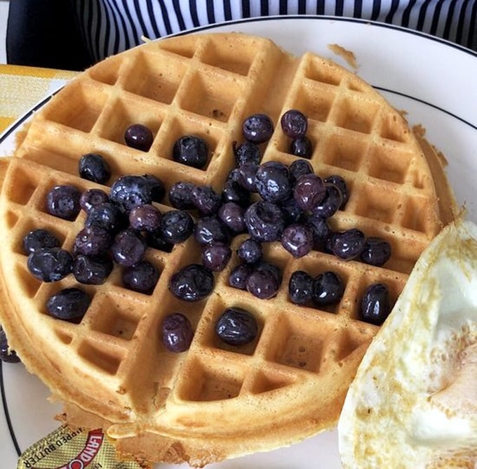 A waffle that's achieved perfect geometry—crisp exterior, fluffy interior, and blueberries that burst like tiny flavor bombs with each forkful.