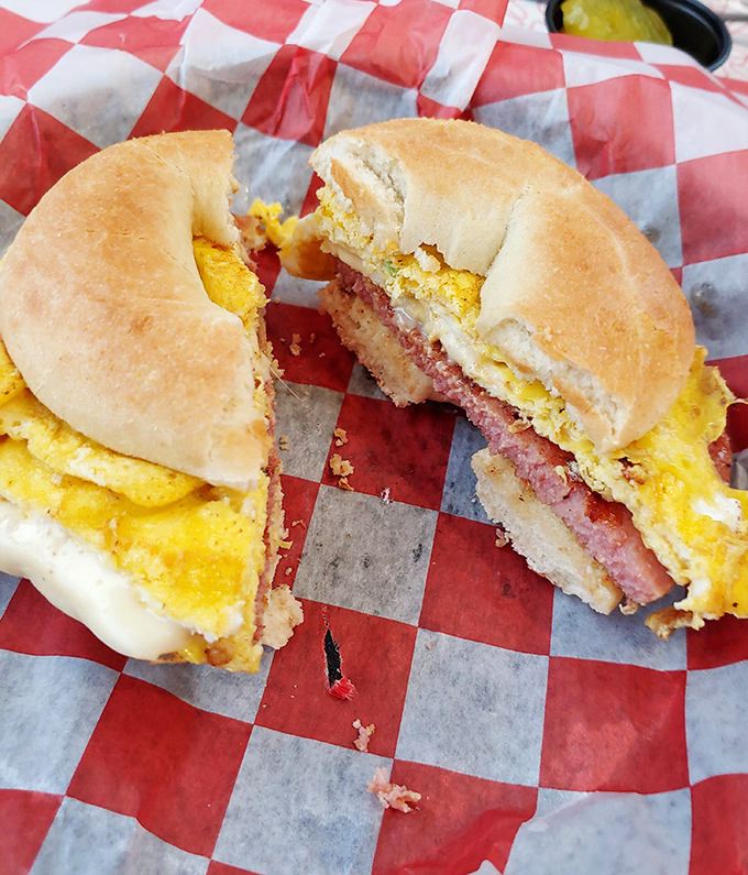 The breakfast sandwich in its natural habitat – a red checkered wrapper. That cross-section reveals the holy trinity: fluffy egg, melty cheese, and savory meat.