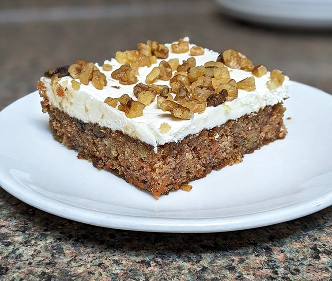 Carrot cake topped with walnuts and cream cheese frosting—proof that vegetables can absolutely count as dessert when properly motivated with sugar.