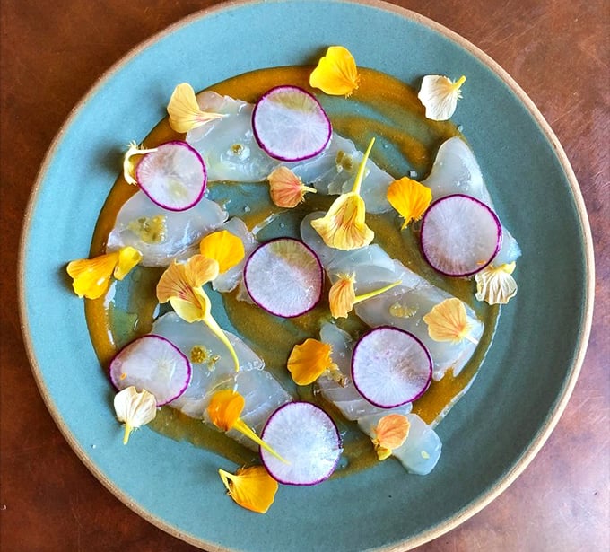 A crudo so beautiful it could hang in a gallery. Translucent fish adorned with vibrant radishes and edible flowers—the ocean reimagined as art.