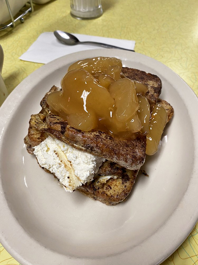 French toast elevated to art form, with cinnamon-kissed bread supporting a mountain of apple compote and cream cheese that would make angels weep.
