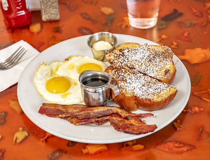 Sweet meets savory in this breakfast symphony: challah French toast dusted with powdered sugar alongside sunny-side-up eggs and bacon.