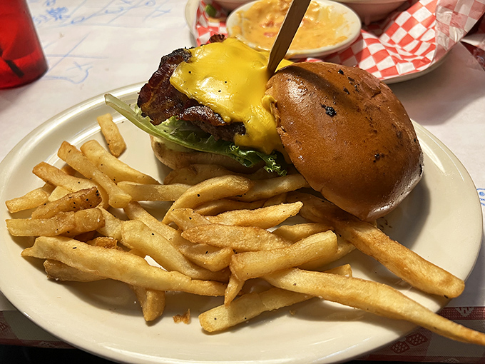 A cheeseburger that requires a game plan before the first bite, accompanied by fries that achieve that mythical balance between crispy exterior and fluffy interior.