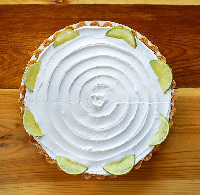 Key lime pie with a spiral of whipped cream so precise it could qualify as art. The lime wedges aren't just garnish—they're a promise of tangy perfection.