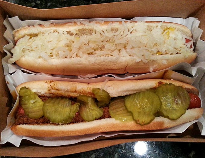 The dynamic duo: one topped with tangy sauerkraut, another with homemade chili and pickles—proof that hot dogs are nature's perfect canvas.