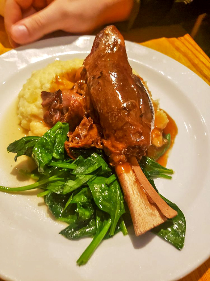 The legendary lamb shank in its natural habitat—falling off the bone and surrounded by greens that somehow avoid being mere spectators.
