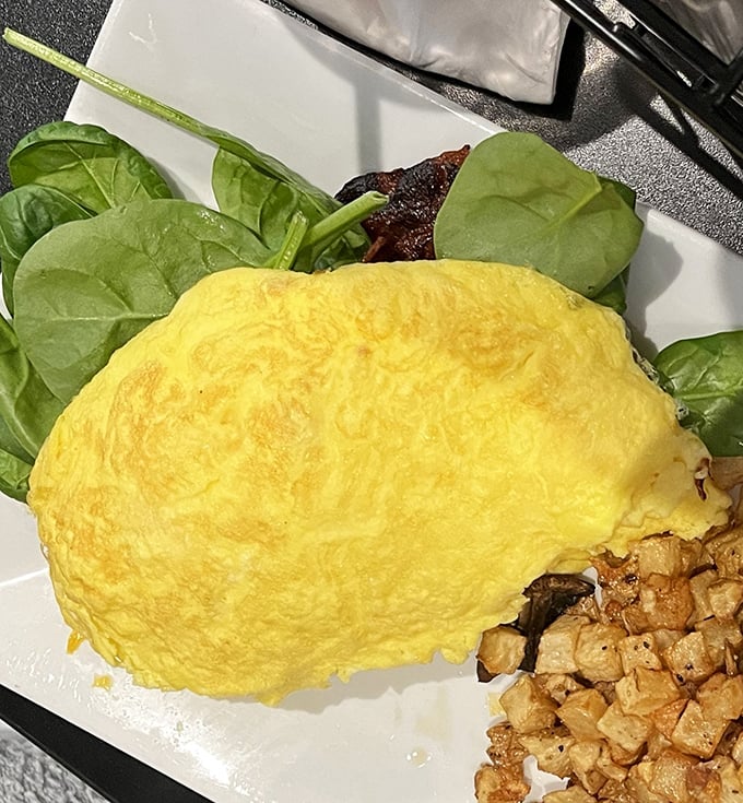 This omelet doesn't just sit on the plate – it lounges luxuriously, a fluffy yellow pillow of egg perfection alongside crispy breakfast potatoes.