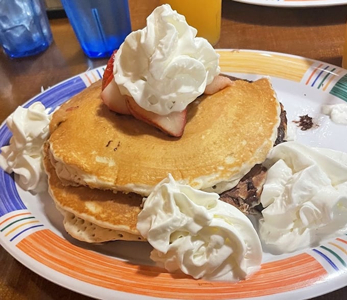 These pancakes aren't just stacked—they're architectural achievements topped with whipped cream islands and strawberry treasures.