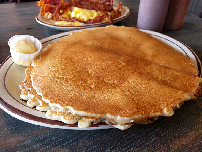 A pancake so perfectly golden it deserves its own California zip code—stretching to the plate's edge with a side of butter melting into breakfast bliss.
