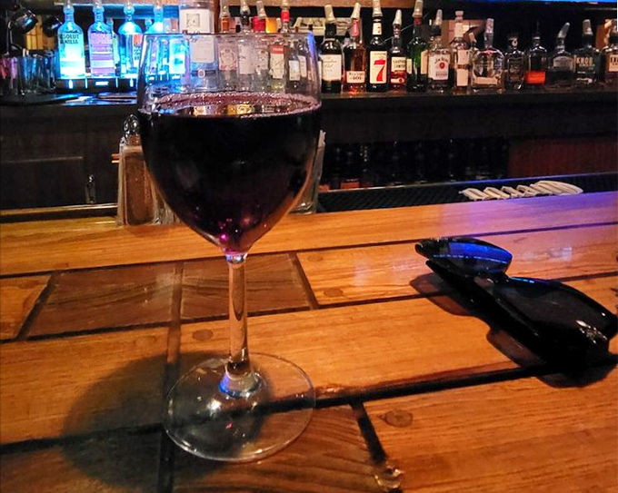 A glass of pinot noir catching the bar light just right—like liquid ruby waiting to complement whatever beef masterpiece you've ordered.