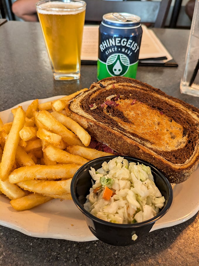 That's not just a sandwich – it's a marbled rye masterpiece with what looks like proper Reuben fillings, accompanied by the holy trinity of fries, slaw, and beer.