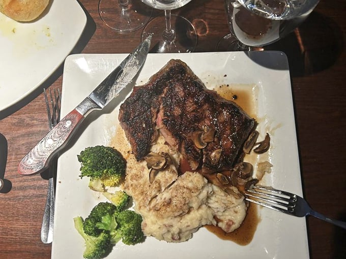 A perfectly seared ribeye lounging on a bed of mashed potatoes with broccoli standing guard. Mushrooms add an earthy supporting cast.